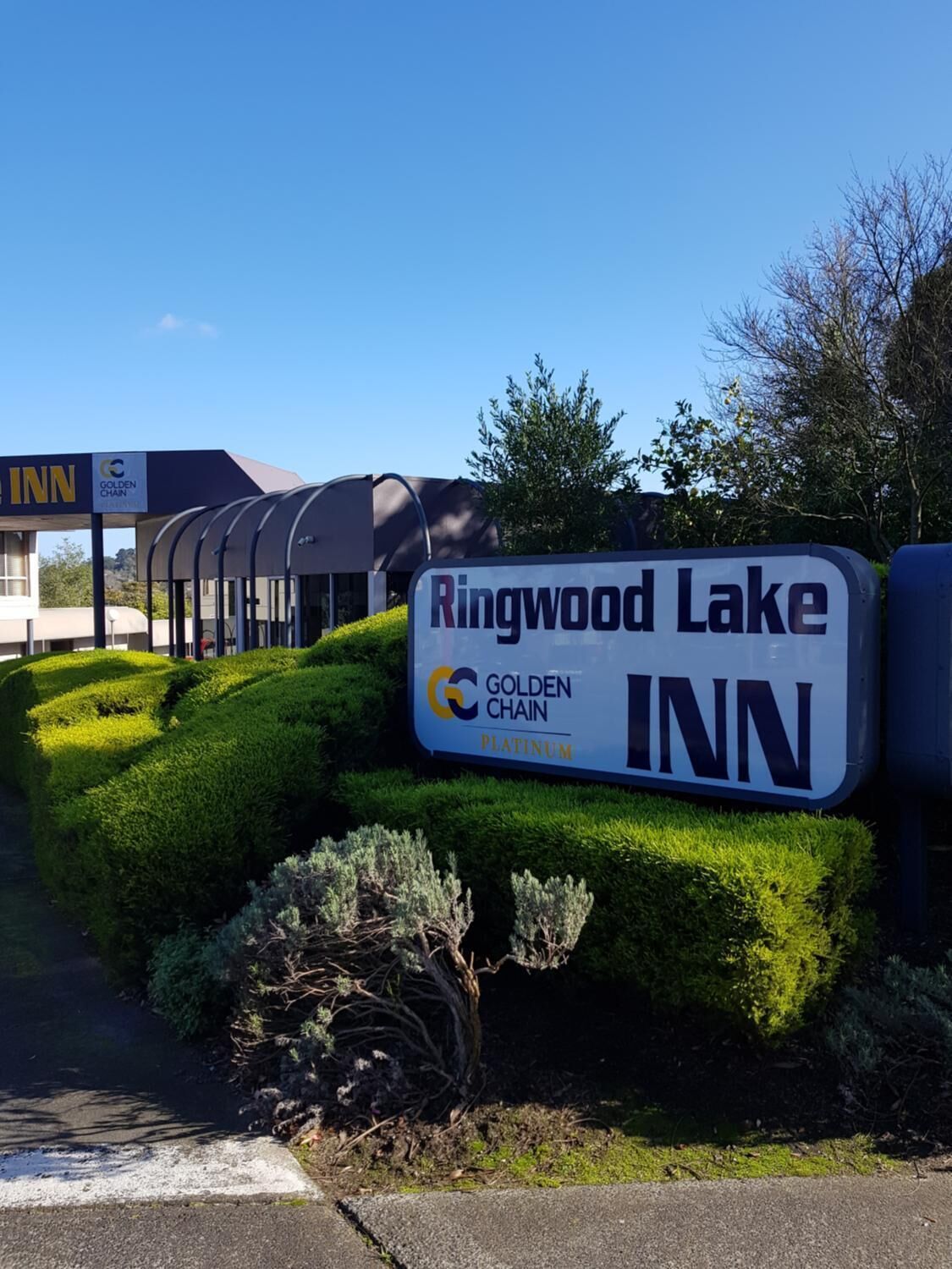 Placa do Ringwood Lake Inn, parte da rede de hotéis Golden Chain Platinum, com céu claro e paisagismo bem cuidado.