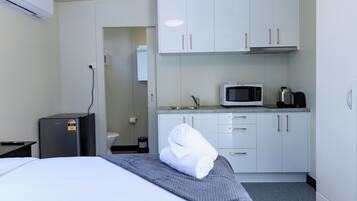 Quarto de hotel com cama, mini-geladeira, micro-ondas, chaleira e pia na cozinha compacta.