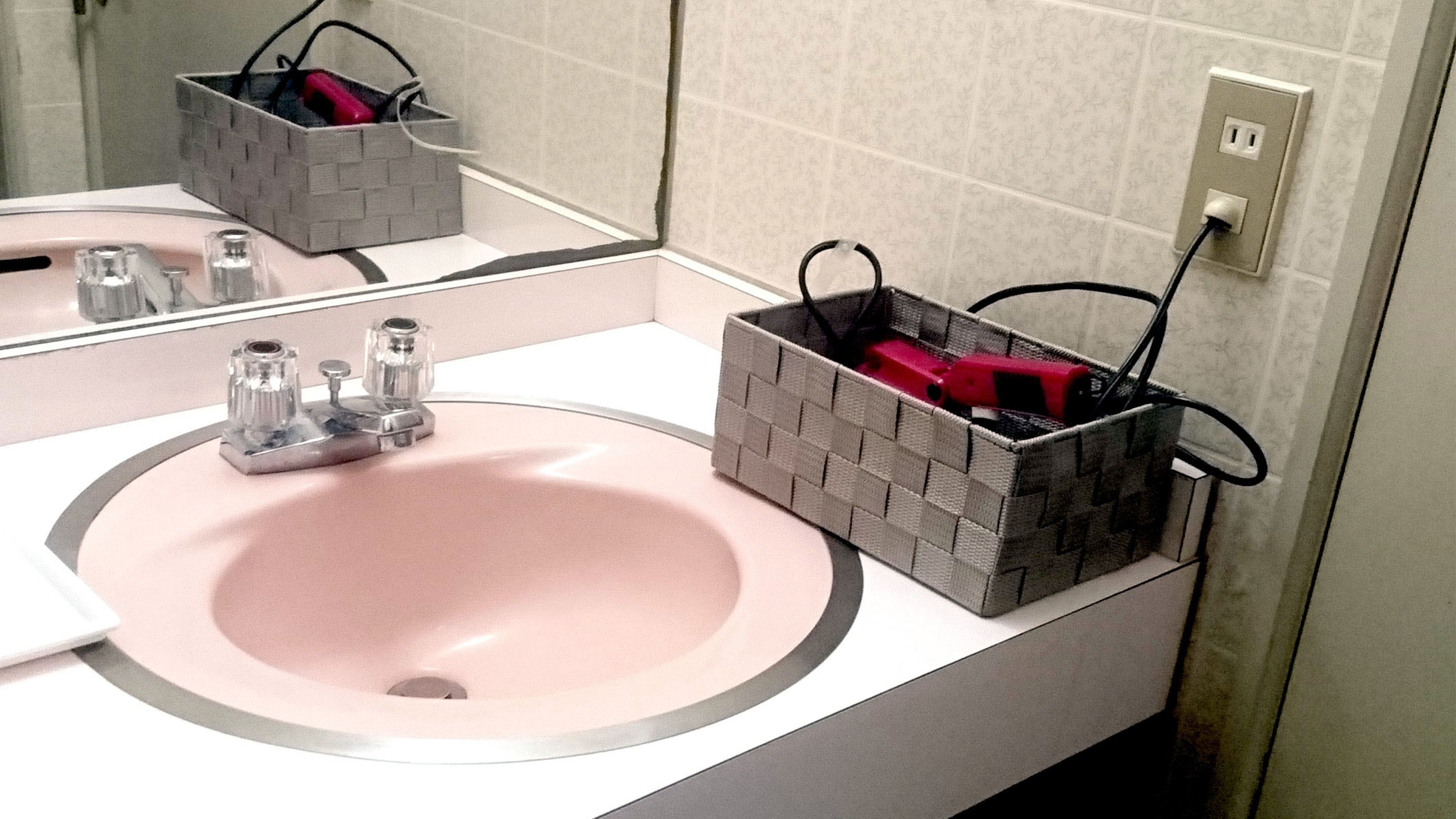 Um banheiro com uma pia rosa, um espelho e duas cestas na bancada.