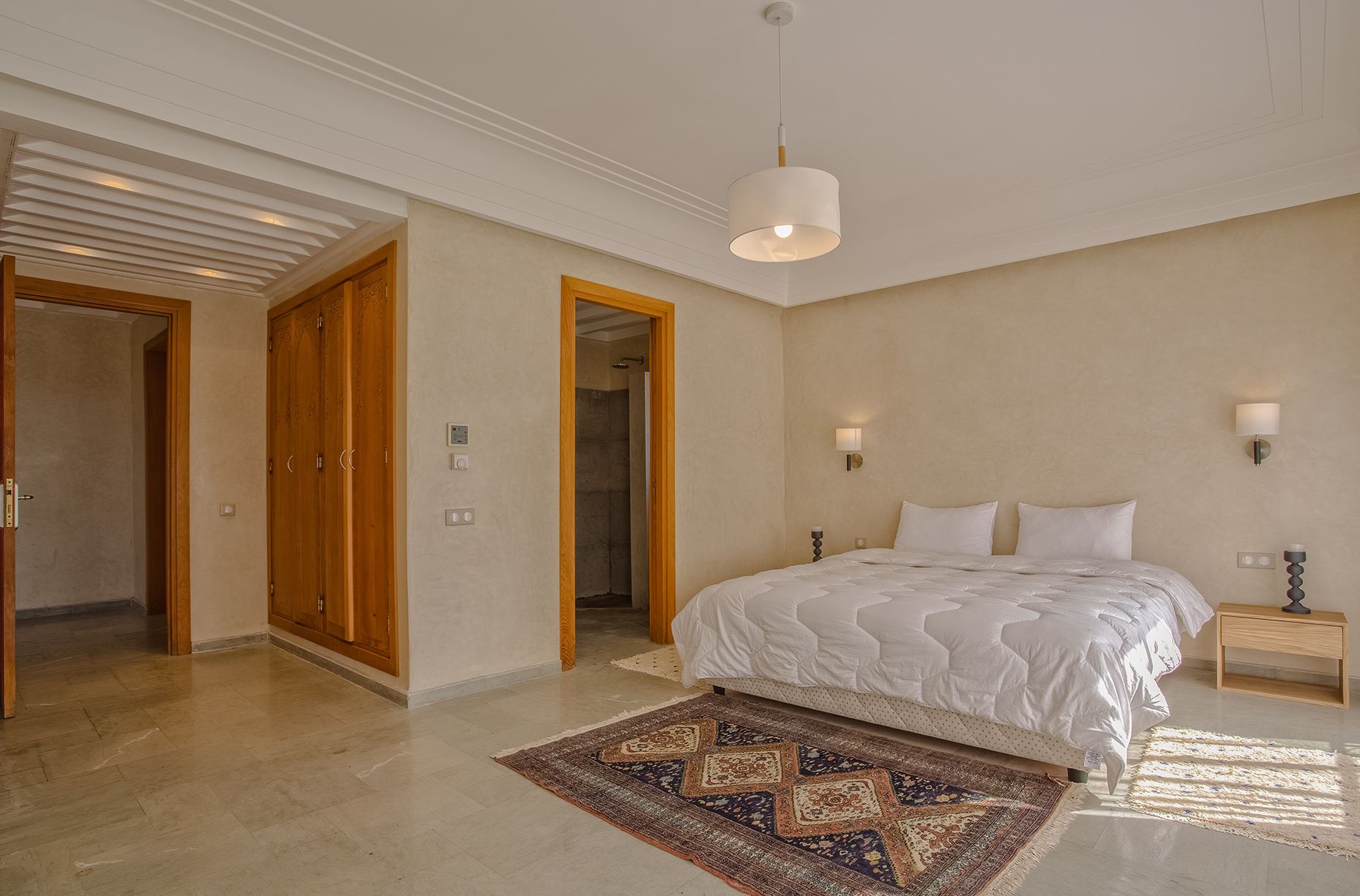 Quarto com cama grande, guarda-roupa de madeira, mesa de cabeceira e luminária no teto.