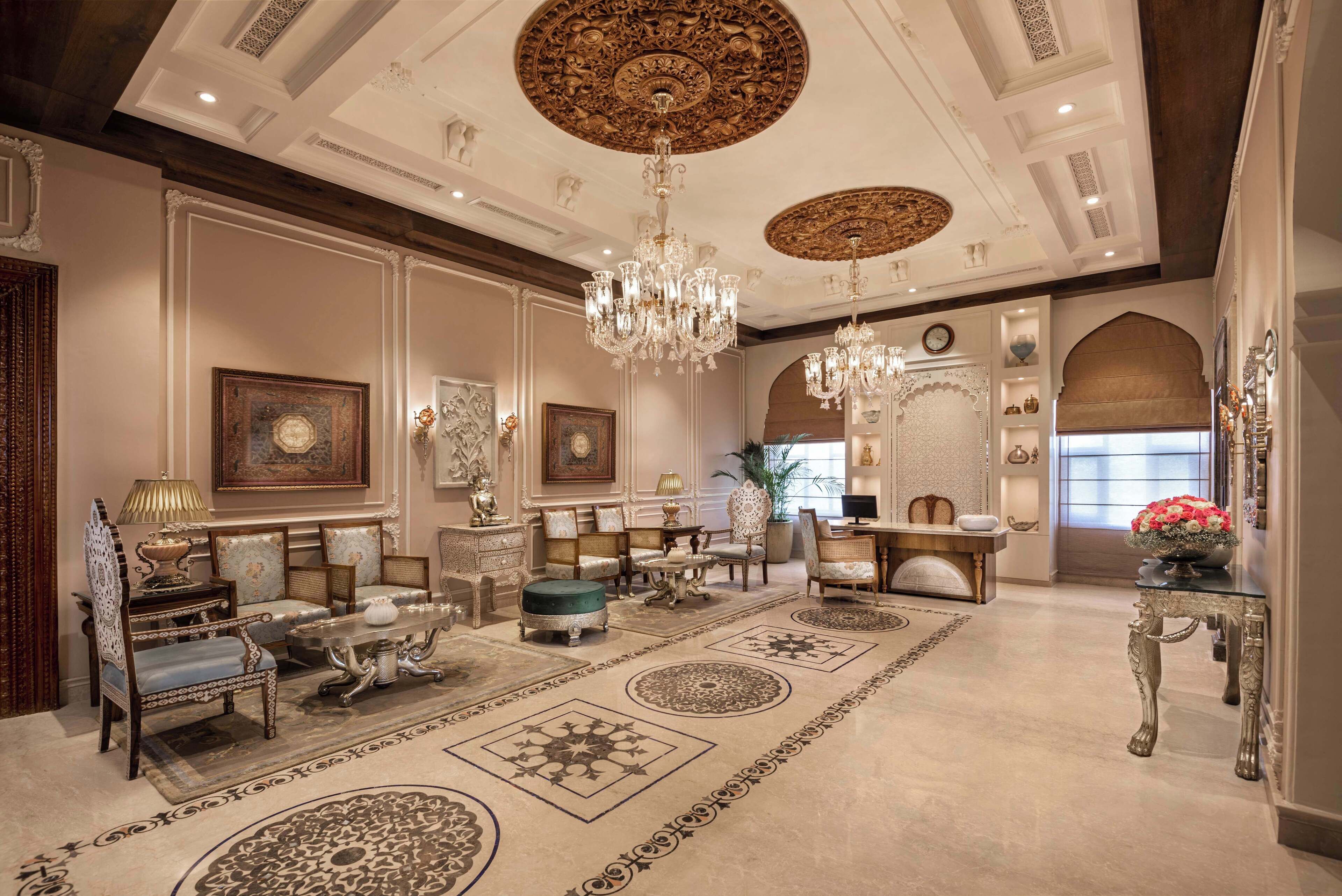 Um hall de entrada luxuoso com lustres elaborados, assentos confortáveis e uma escadaria imponente.