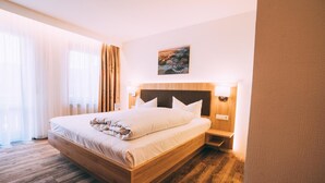 Quarto de hotel moderno com cama de madeira, roupa de cama branca, um quadro na parede e uma janela grande com cortinas.