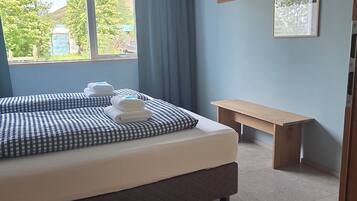 Quarto com cama, um banquinho, janela com vista e prateleira na parede.