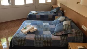 Quarto de hotel com duas camas, cada uma com colcha e almofadas xadrez. Há uma mesa de cabeceira de madeira com uma luminária e um controle remoto.