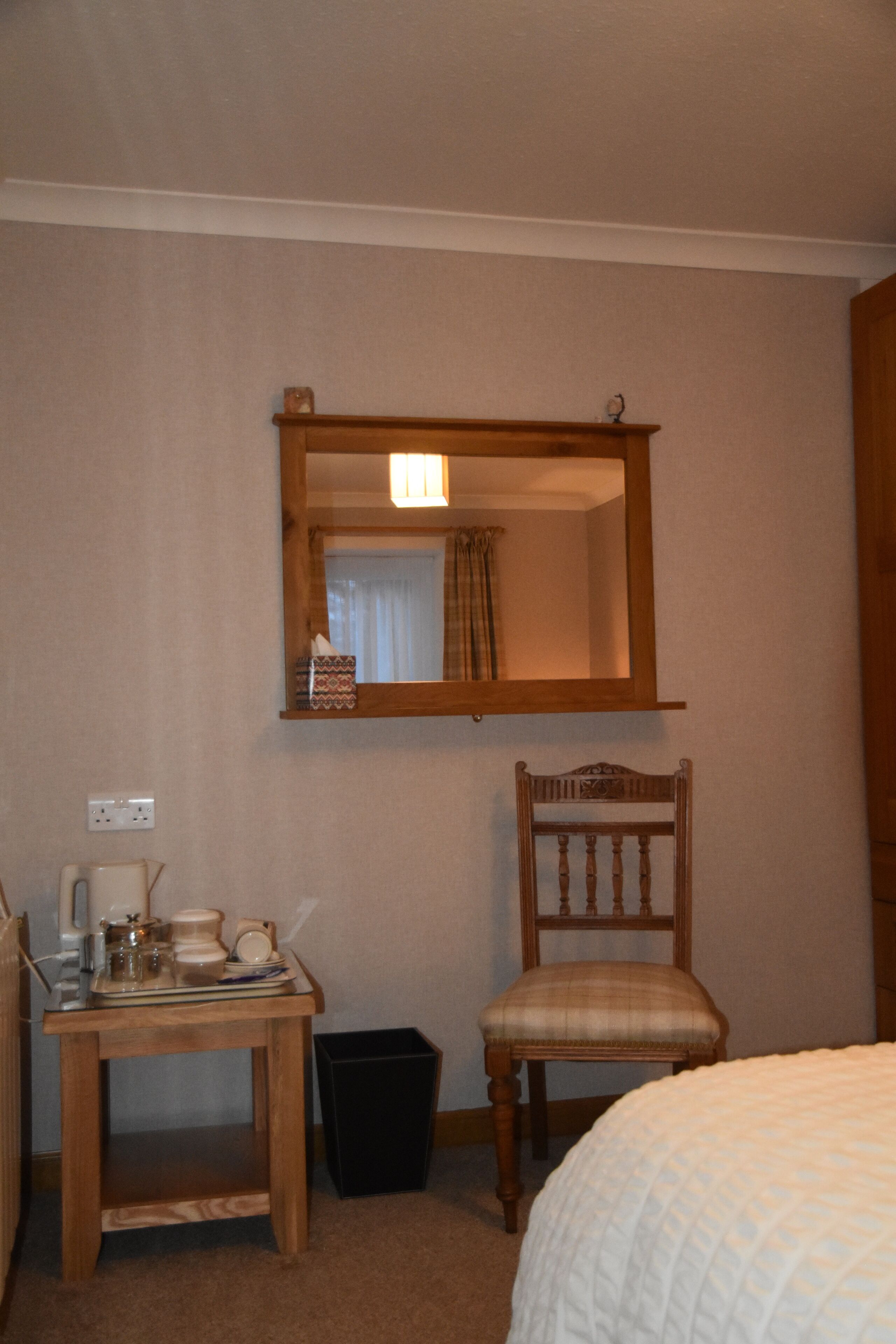 Quarto de hotel com escrivaninha de madeira, uma cadeira, uma cama e um espelho na parede.