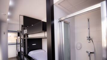 Quarto de hotel moderno com beliches, chuveiro e vista da cidade.