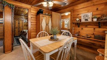 Interior acolhedor de uma cabana com mesa de jantar, cadeiras, ventilador de teto e decoração com tema de urso.