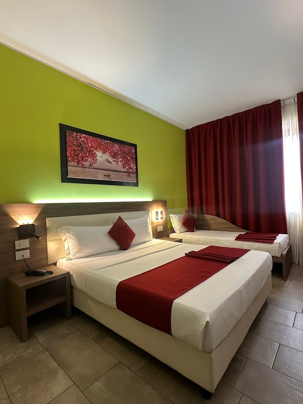 Quarto de hotel com duas camas, uma mesinha de cabeceira com telefone, uma luminária na parede e um quadro de uma árvore vermelha.