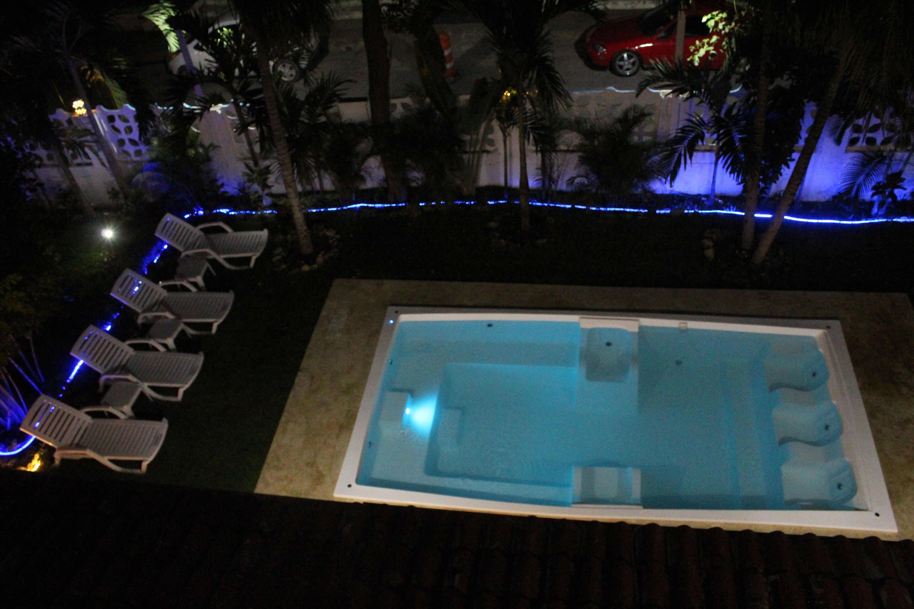 Piscina externa com espreguiçadeiras e luzes LED azuis.