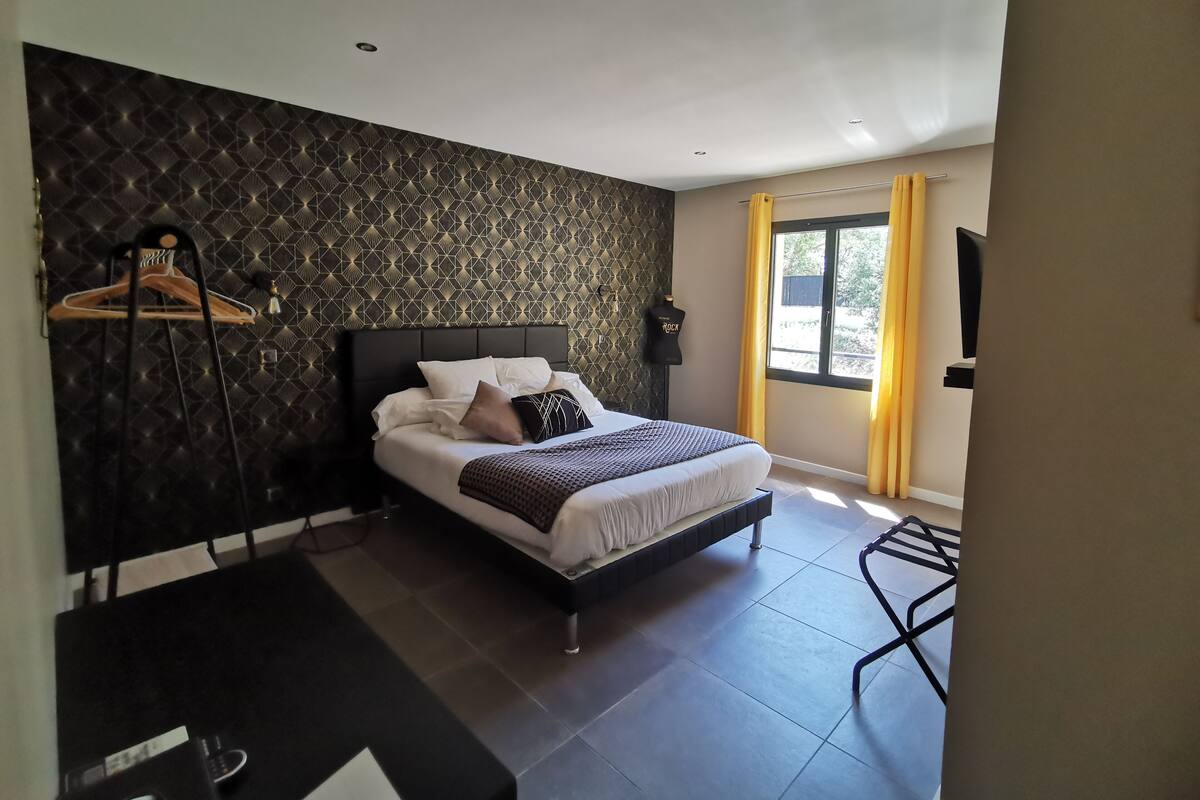 Quarto moderno com cama, luminária pendente, cabideiro e janela com cortinas.