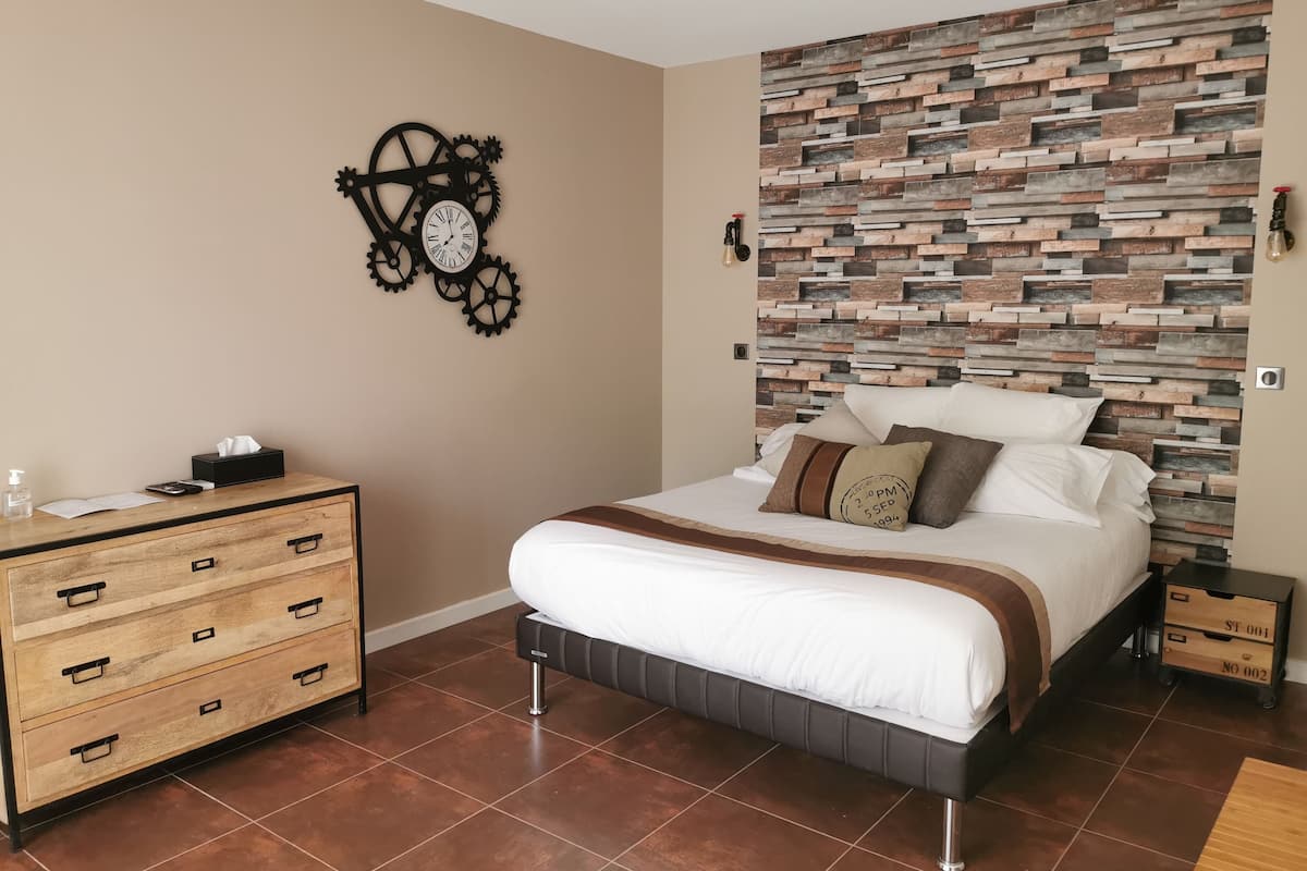 Um quarto com cama, cômoda de madeira, relógio de parede e painel decorativo.