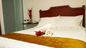 Cama bem arrumada com lençóis brancos, um cobertor marrom e uma toalha enrolada.