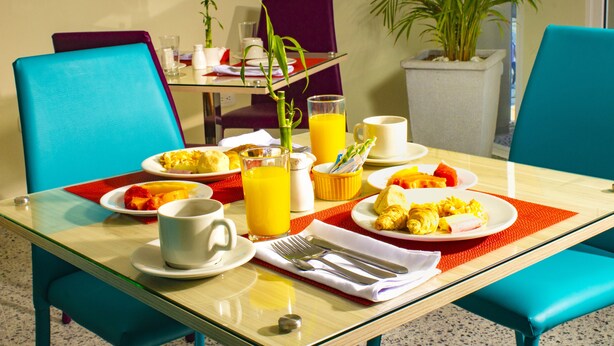 Uma mesa de café da manhã posta com pratos de comida, um copo de suco de laranja e uma xícara de café.