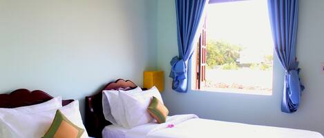 Quarto com duas camas, janela com cortinas azuis e vista para o verde lá fora.