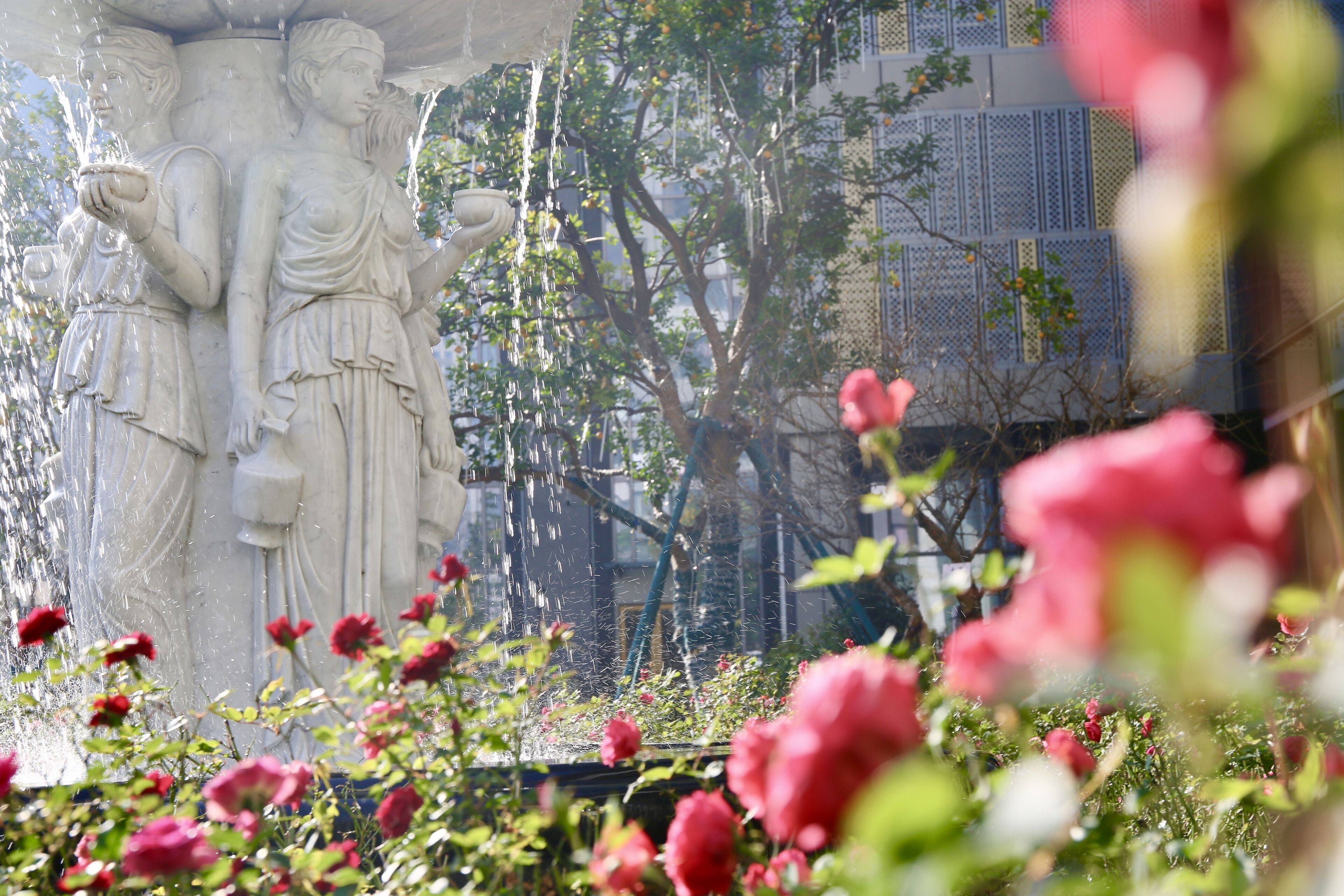 Uma estátua com água jorrando da base, rodeada por vegetação e flores.
