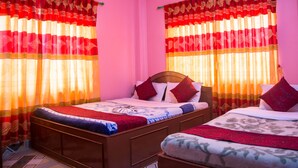 Quarto de hotel com duas camas, cada uma com cabeceira de madeira, e uma janela grande com cortinas vermelhas e amarelas.