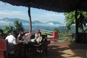 Um grupo de pessoas jantando em uma mesa ao ar livre com vista para montanhas e nuvens.