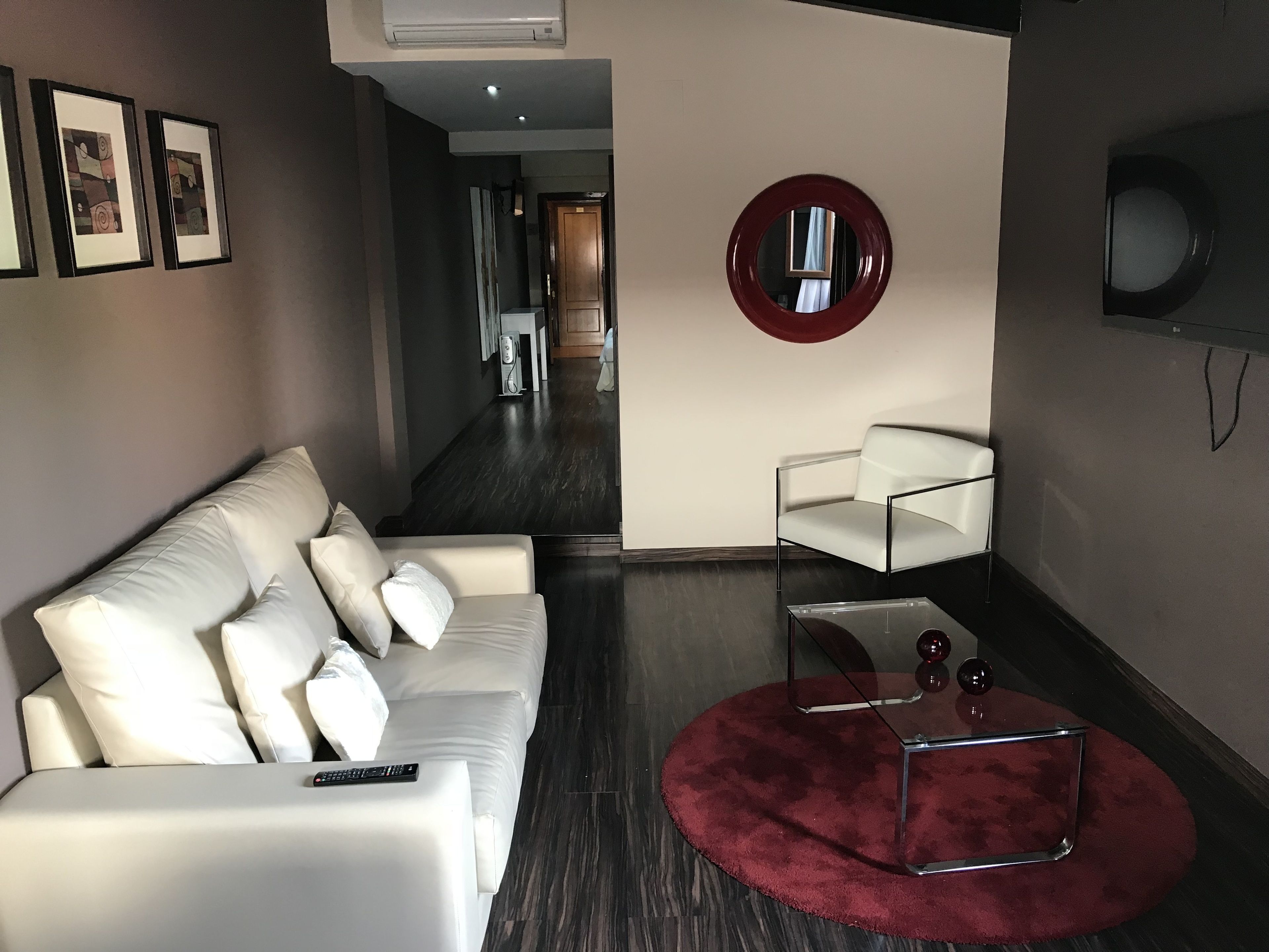 Uma sala de estar moderna com um sofá branco, um tapete redondo vermelho e uma mesa de centro de vidro.