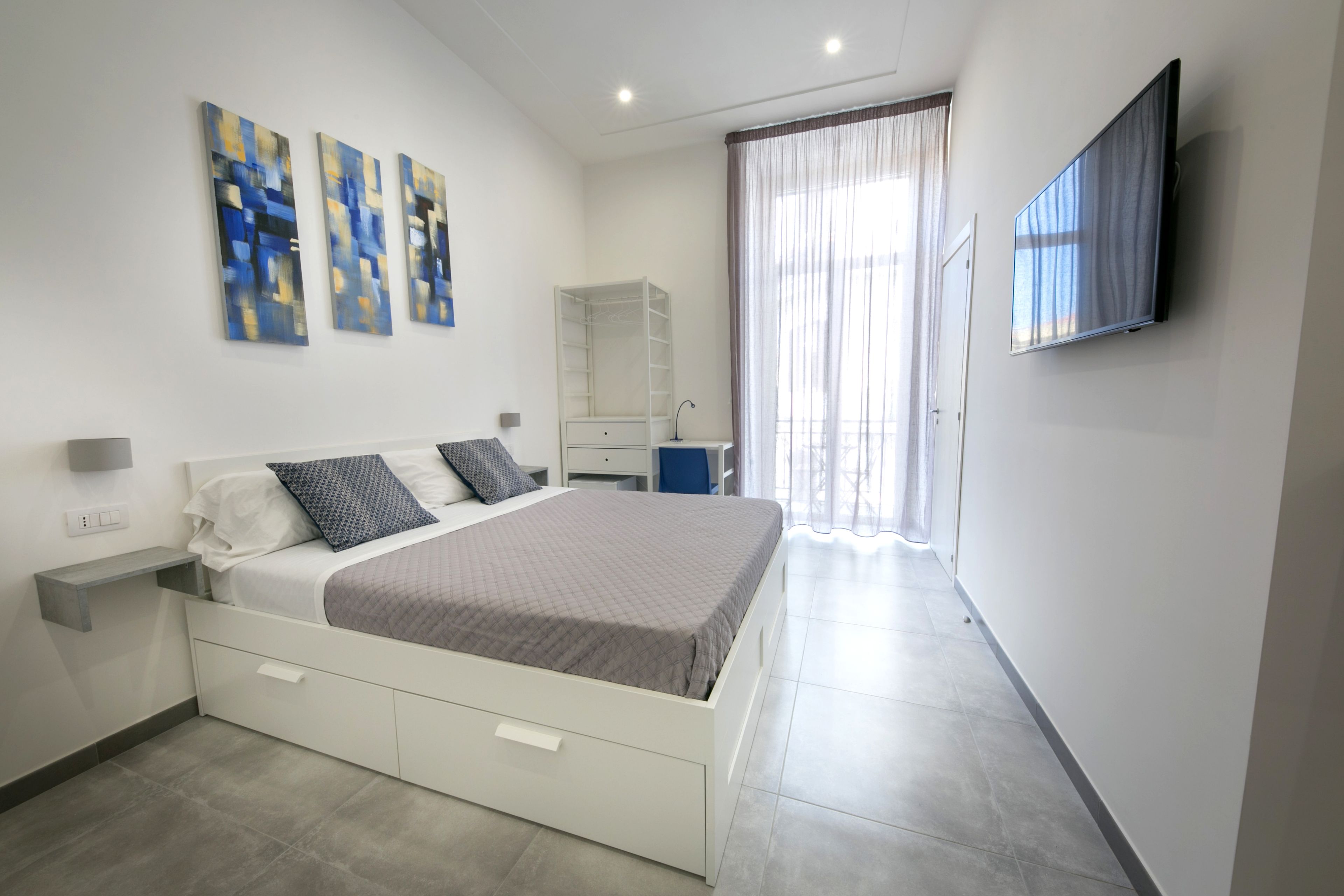 Quarto moderno com cama, mesas de cabeceira, guarda-roupa, televisão e arte abstrata nas paredes.