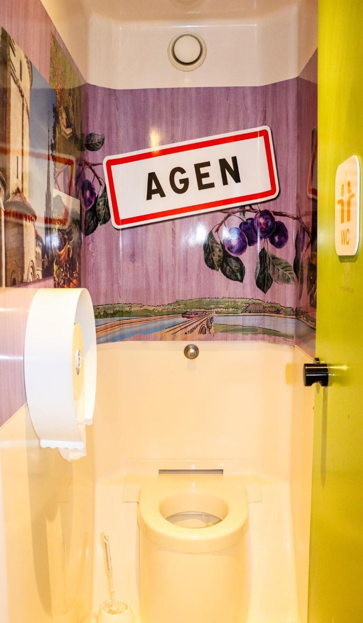 Um banheiro com vaso sanitário, secador de mãos e uma placa na parede com a inscrição 'AGEN'.