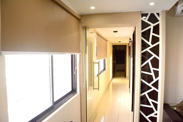 Corredor de hotel com porta de vidro, parede bege e painel decorativo branco.
