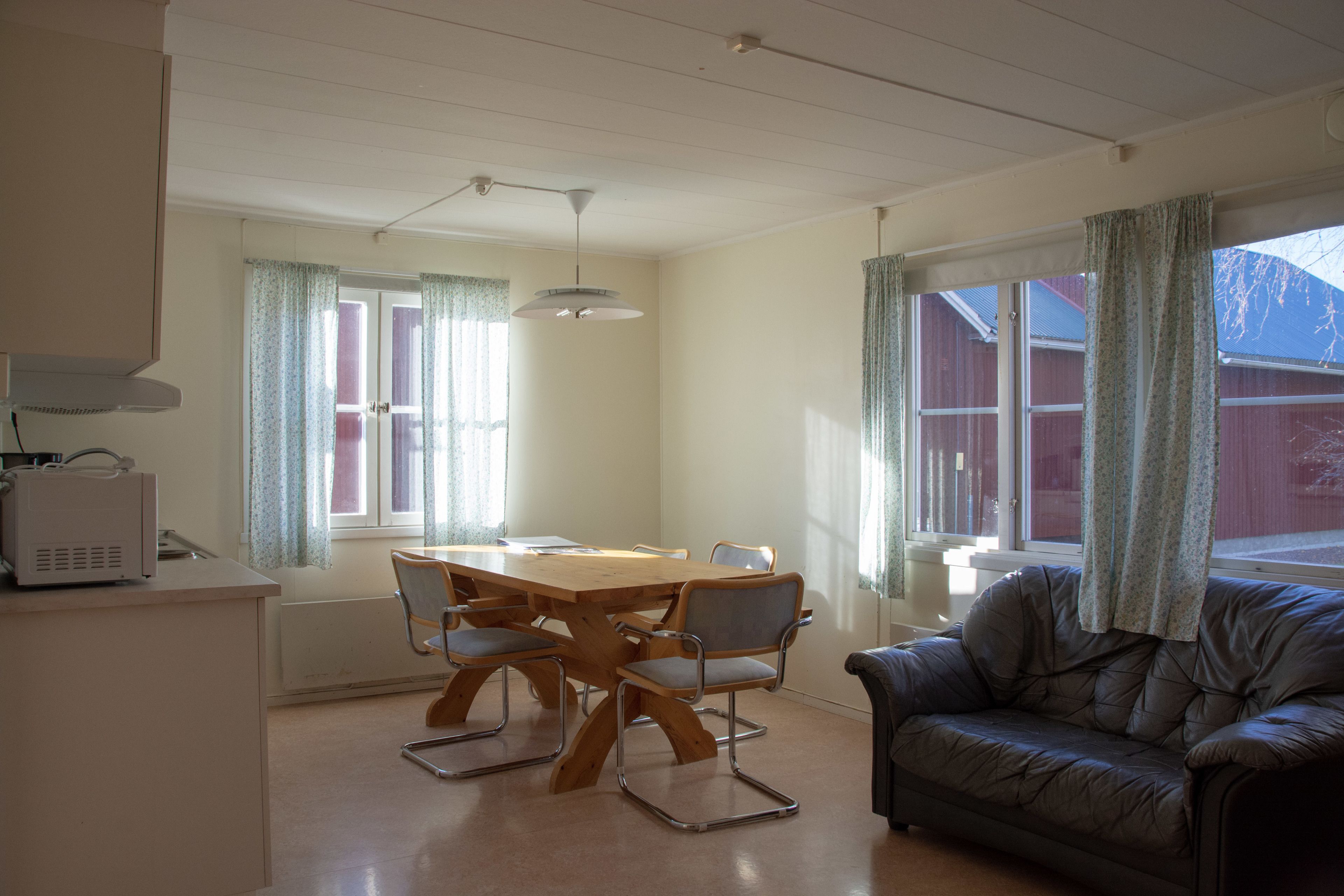 Uma sala de jantar com mesa e cadeiras de madeira, um sofá de couro e uma janela com cortinas.
