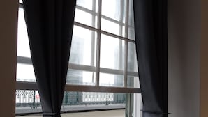 Uma janela com cortinas pretas, vista de um edifício com varanda e uma placa de rua.