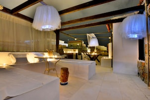 Um interior acolhedor e bem iluminado, com área de estar, mesas e luminárias pendentes.
