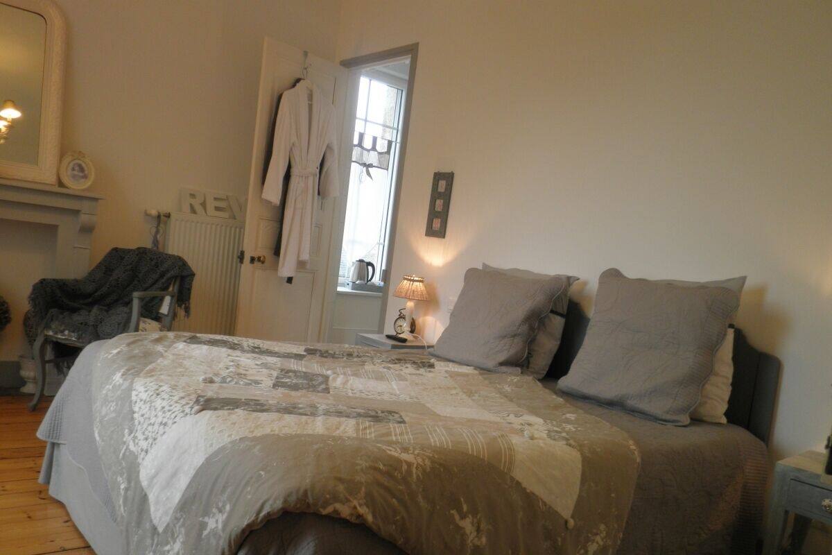 Quarto com cama grande, mesa de cabeceira, abajur, cadeira e roupão pendurado na porta.