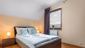 Quarto com cama de madeira, mesa de cabeceira com luminária, janela com vista para as montanhas e radiador.
