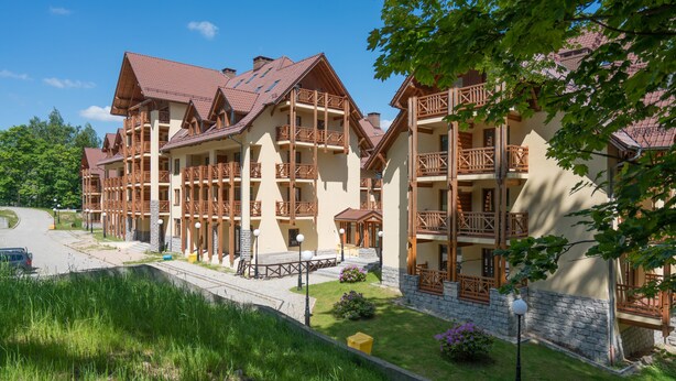Um hotel com várias andares, varandas, fachada de pedra e um jardim bem cuidado.