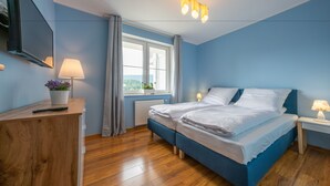 Quarto com cama de casal, cómoda de madeira, janela com cortinas e luminária no teto.