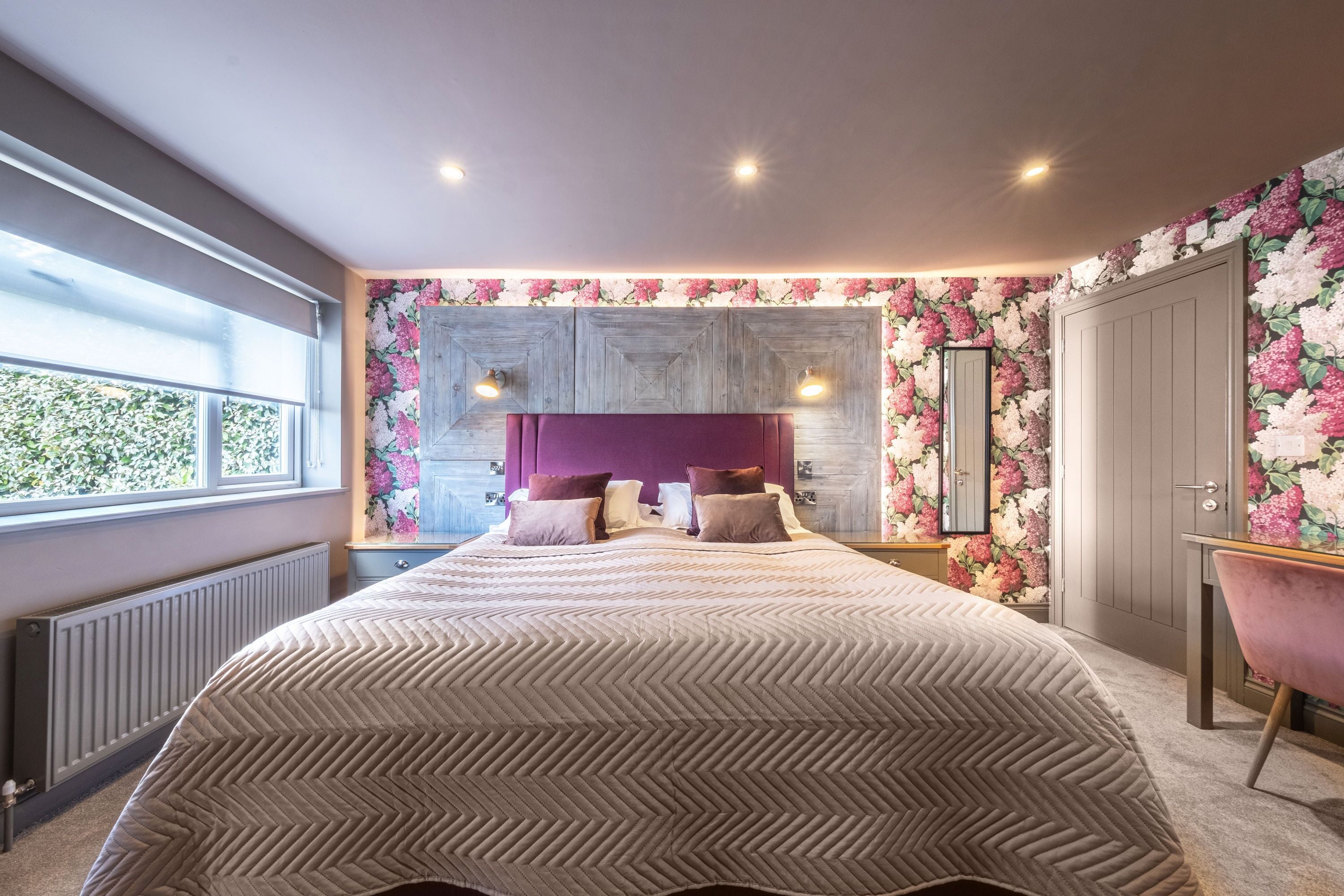 Quarto com cama grande, penteadeira, espelho e janela com vista para o verde.