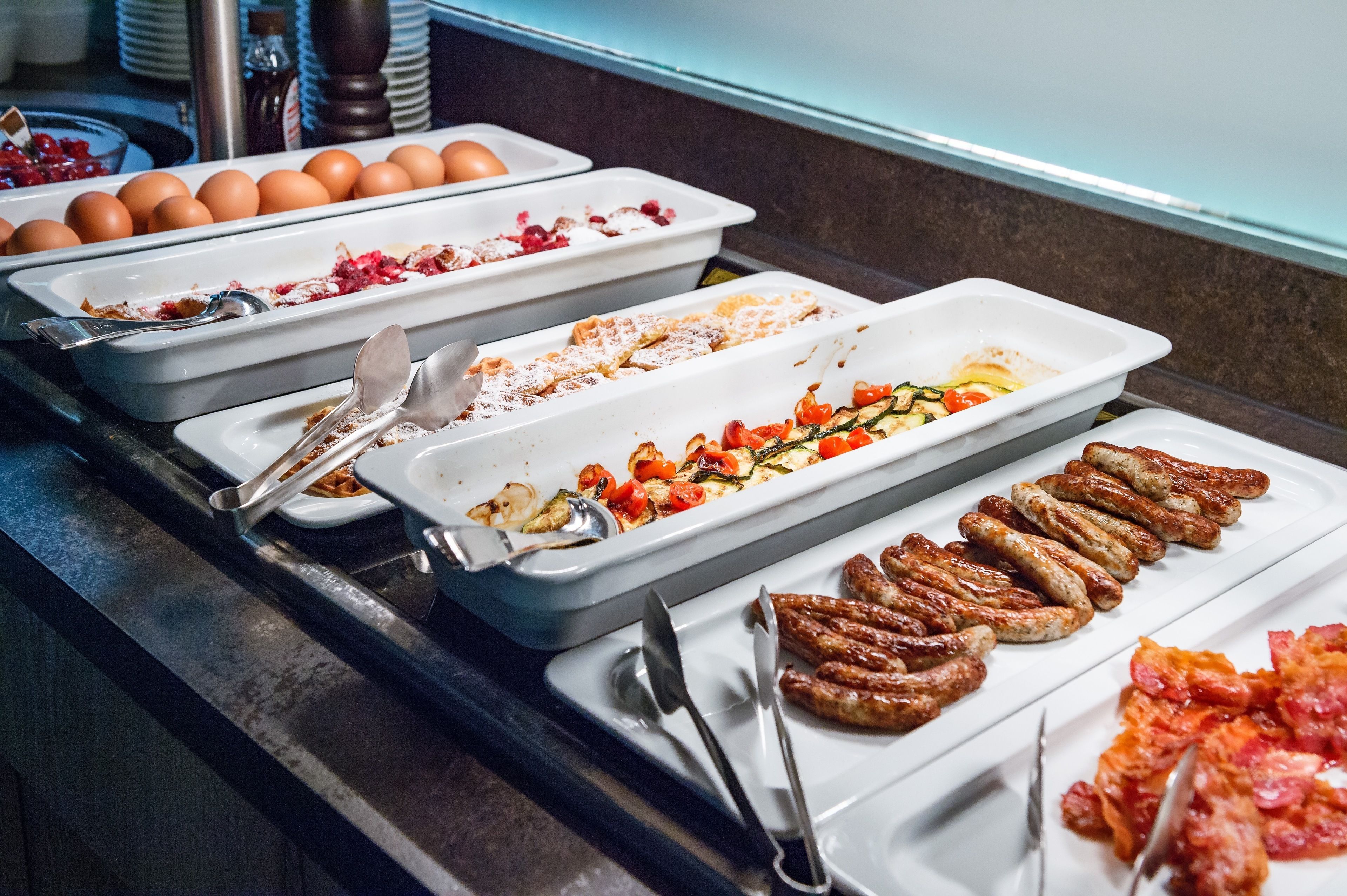 Buffet com diversas opções de comida, incluindo ovos, legumes e linguiça.