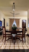 Uma sala de jantar com uma mesa redonda, quatro cadeiras, um ventilador de teto e uma taça decorativa sobre a mesa.