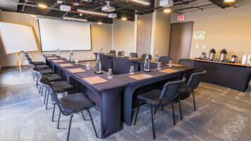 Uma sala de conferências com uma mesa comprida, cadeiras, um quadro branco e um projetor.