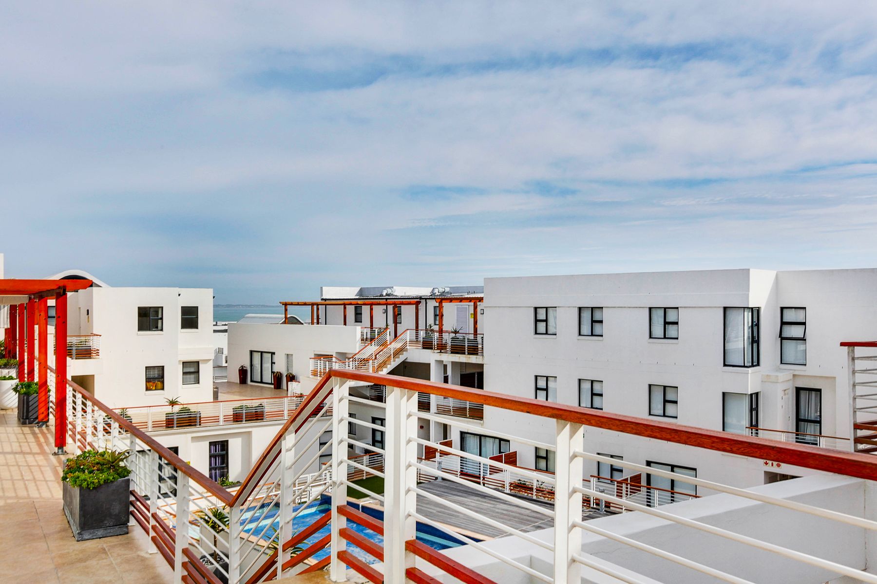 Um edifício moderno com vários andares, uma escadaria com corrimão vermelho e vista para o mar.