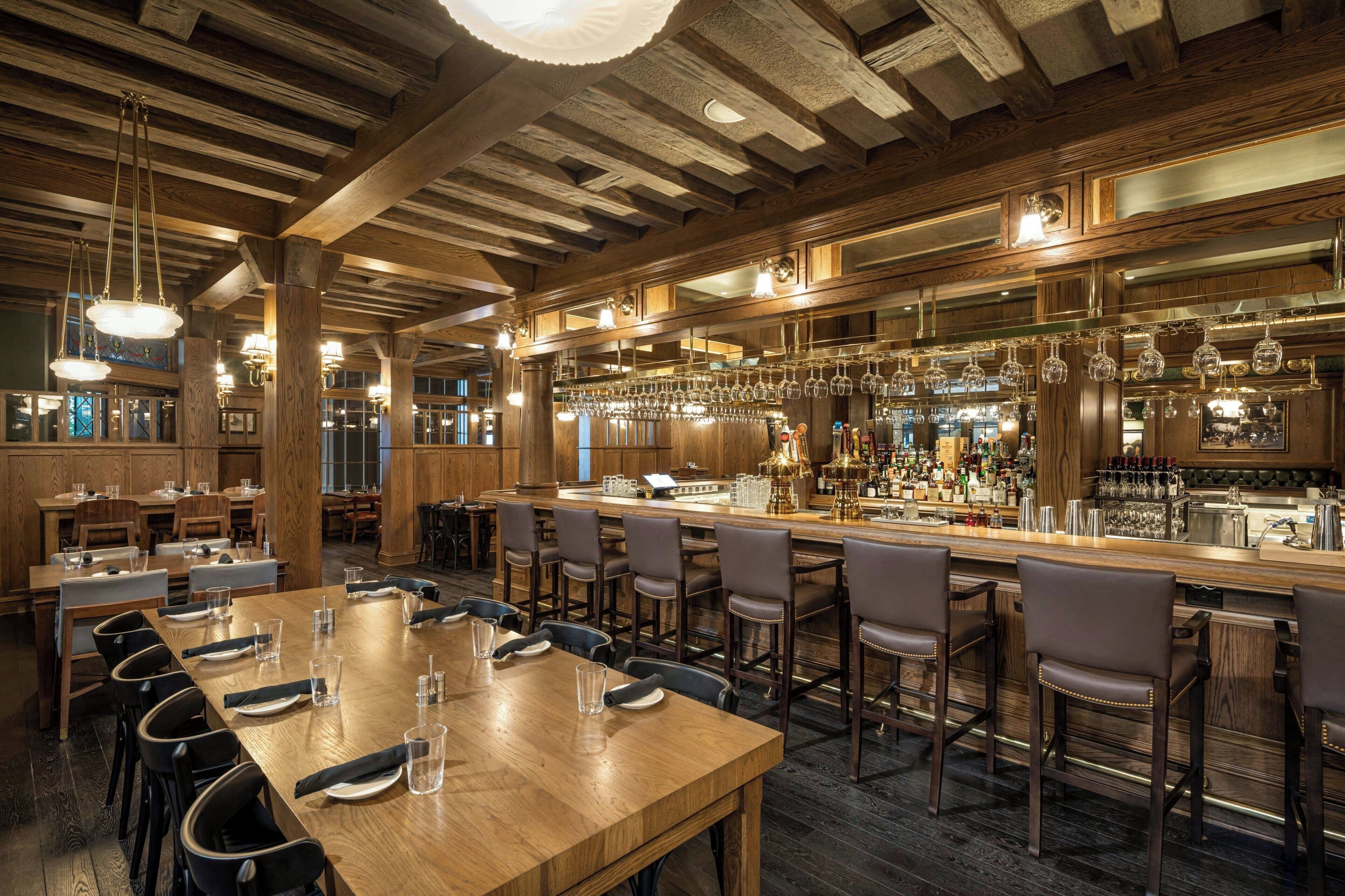 Uma área de bar com vigas de madeira, um balcão comprido e várias luminárias pendentes.