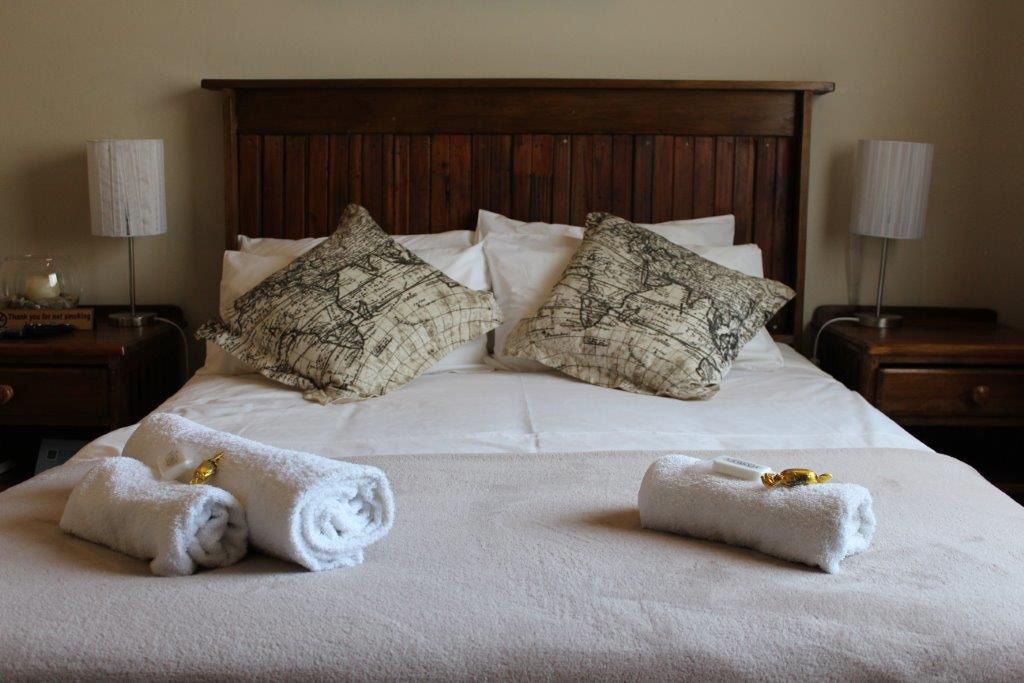 Cama bem arrumada com duas almofadas decorativas, um par de abajures e toalhas dobradas sobre a cama.