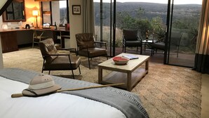 Quarto de hotel com cama, escrivaninha, laptop, cadeira, mesa com tigela e vista para as montanhas.