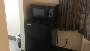 Uma kitchenette compacta com geladeira preta e micro-ondas, uma tomada na parede e uma lixeira no canto.