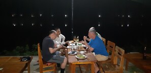 Um grupo de pessoas jantando em uma mesa ao ar livre com vista para o céu noturno.