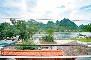 Vista de um rio com montanhas ao fundo, uma ponte e um edifício com telhado vermelho em primeiro plano.