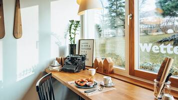 Uma zona de refeições moderna com uma mesa de madeira, uma cadeira preta, um candeeiro pendente e uma janela com vista para vegetação.