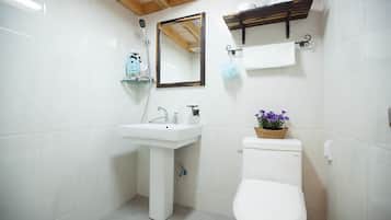 Casa de banho com lavatório branco, sanita, espelho e um prateleira com artigos de higiene pessoal.