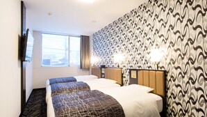 Quarto de hotel com duas camas, televisão, janela, papel de parede estampado e luminárias fixadas na parede.