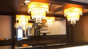 Uma área de recepção de hotel com lustres, um balcão de recepção e uma placa exibindo o nome do hotel e informações de contato.