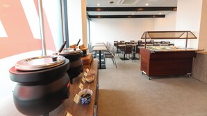 Buffet montado com várias estações de serviço, um balcão longo com tigelas e utensílios, e uma área de estar com mesas e cadeiras.