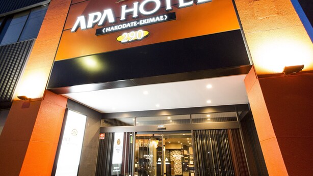 Exterior do APA Hotel com fachada moderna, sinalização iluminada e entrada de vidro.
