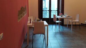 Uma área de refeições com mesa e cadeiras, luminária fixada na parede e janela com vista para o exterior.